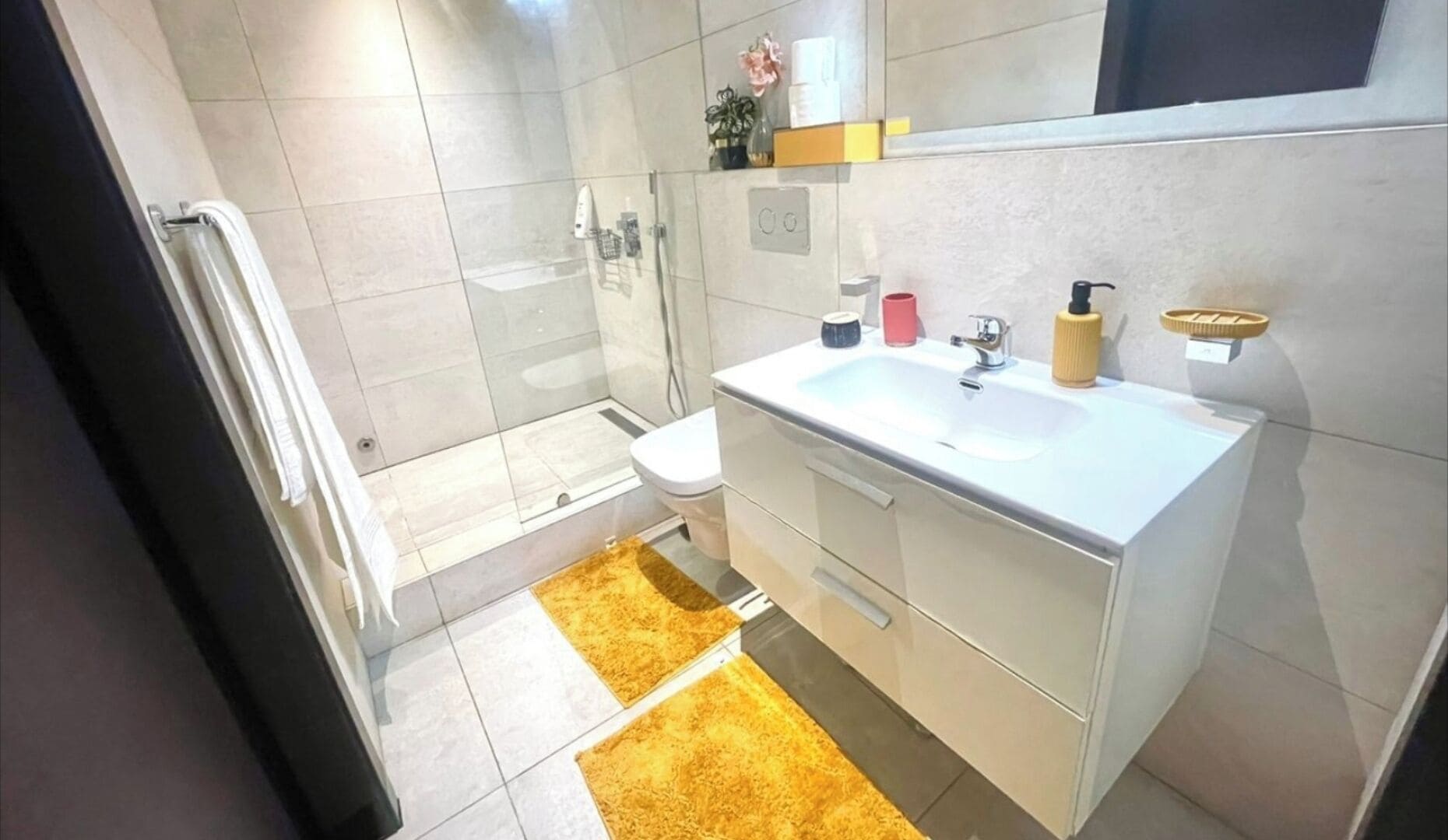 Casa de banho moderna com cabine de chuveiro em vidro, lavatório branco e tapete bege.