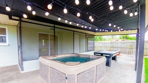 Um pátio externo com hidromassagem, mesa de bilhar e luzes de festa.
