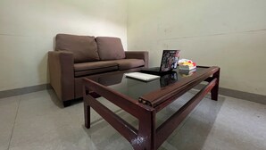 Uma sala de estar com um sofá marrom, uma mesa de centro com tampo de vidro e uma revista sobre a mesa.