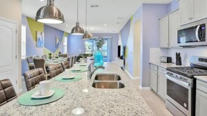 Cozinha moderna com bancadas de granito, eletrodomésticos de aço inoxidável e área de jantar com cadeiras de couro e uma mesa grande.