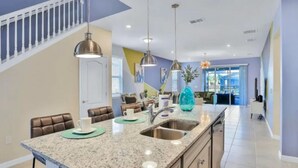 Cozinha moderna com ilha central, eletrodomésticos de aço inoxidável e iluminação pendente.