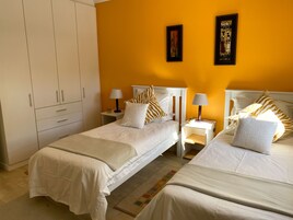 Quarto de hotel com duas camas, roupa de cama branca, almofadas listradas e chão de madeira.