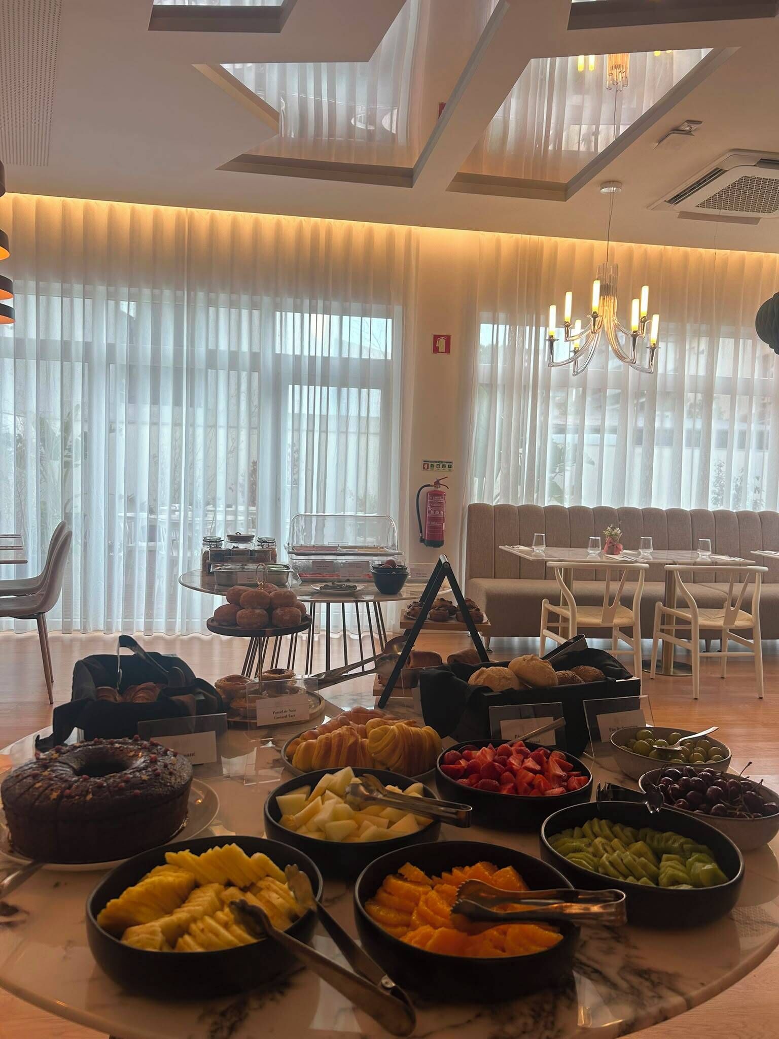 Um buffet de café da manhã com diversos alimentos e uma área de estar com mesas e cadeiras.