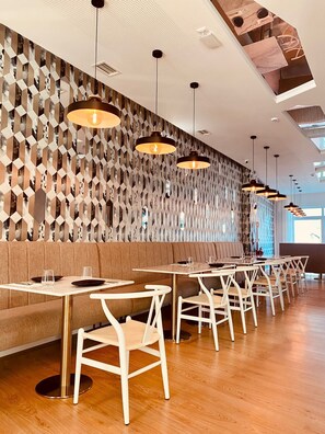 Um interior de restaurante moderno com paredes com padrão geométrico, luminárias pendentes, assentos acolchoados e piso de madeira.