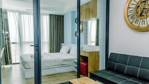 Quarto de hotel moderno com cama, escrivaninha de madeira, sofá de couro preto e um relógio de parede grande.