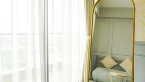Quarto com uma janela grande, espelho, sofá com almofadas e uma mesa decorativa.