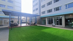 Um pátio com grama sintética, mobiliário externo e uma área coberta com pérgola.