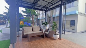 Uma área de estar coberta ao ar livre, com mobiliário de vime e plantas em vasos.