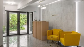 Uma área de recepção moderna, com entrada por porta de vidro, balcão de madeira e duas poltronas amarelas.