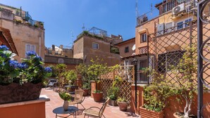 Um pátio com área de estar externa, plantas em vasos e vista para edifícios vizinhos.