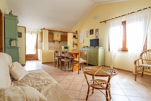 Uma sala de estar acolhedora com sofá, mesa de jantar com cadeiras, cozinha equipada com armários e micro-ondas, e uma televisão.