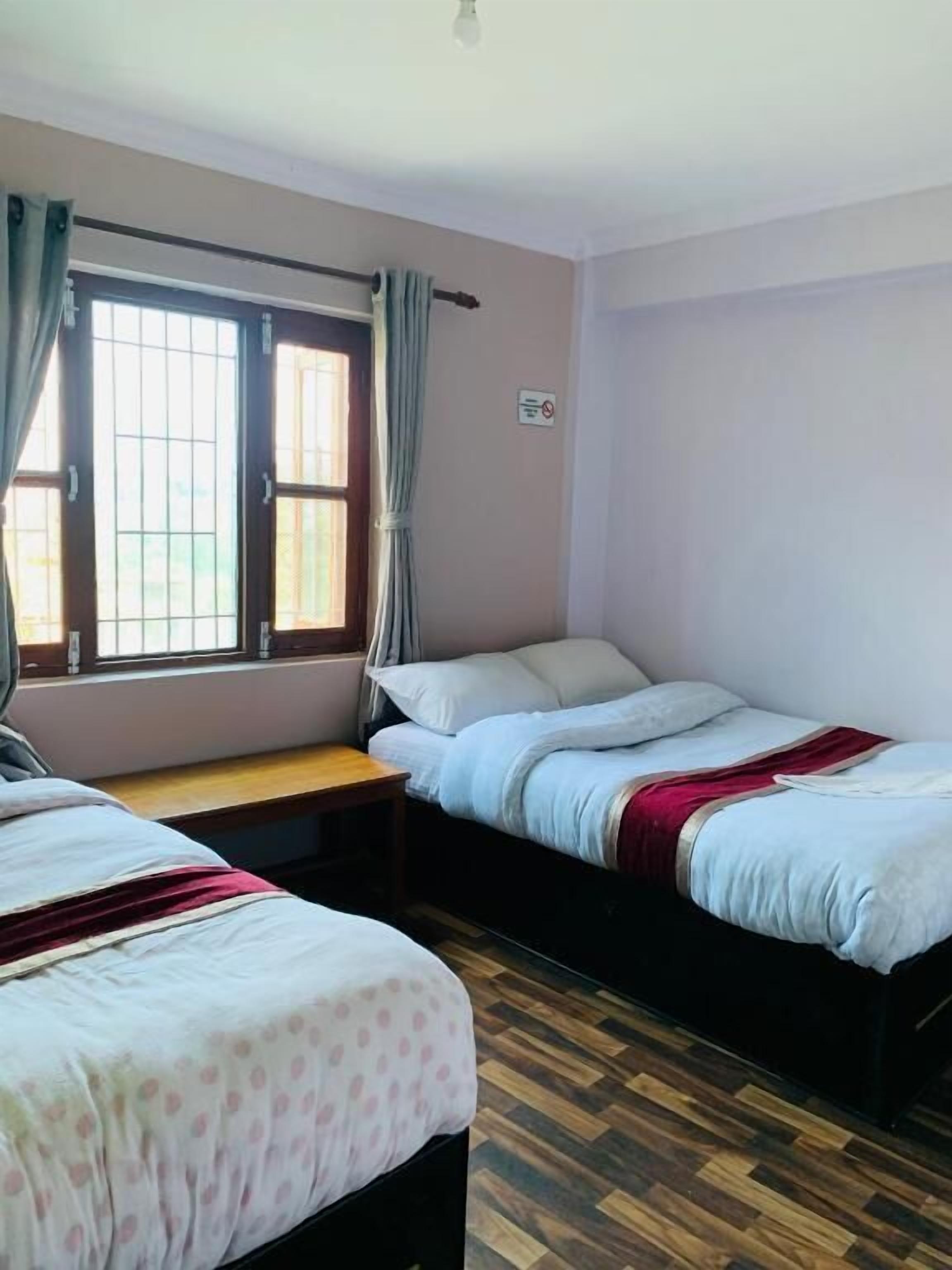 Quarto com duas camas, uma escrivaninha de madeira e uma janela com cortinas.