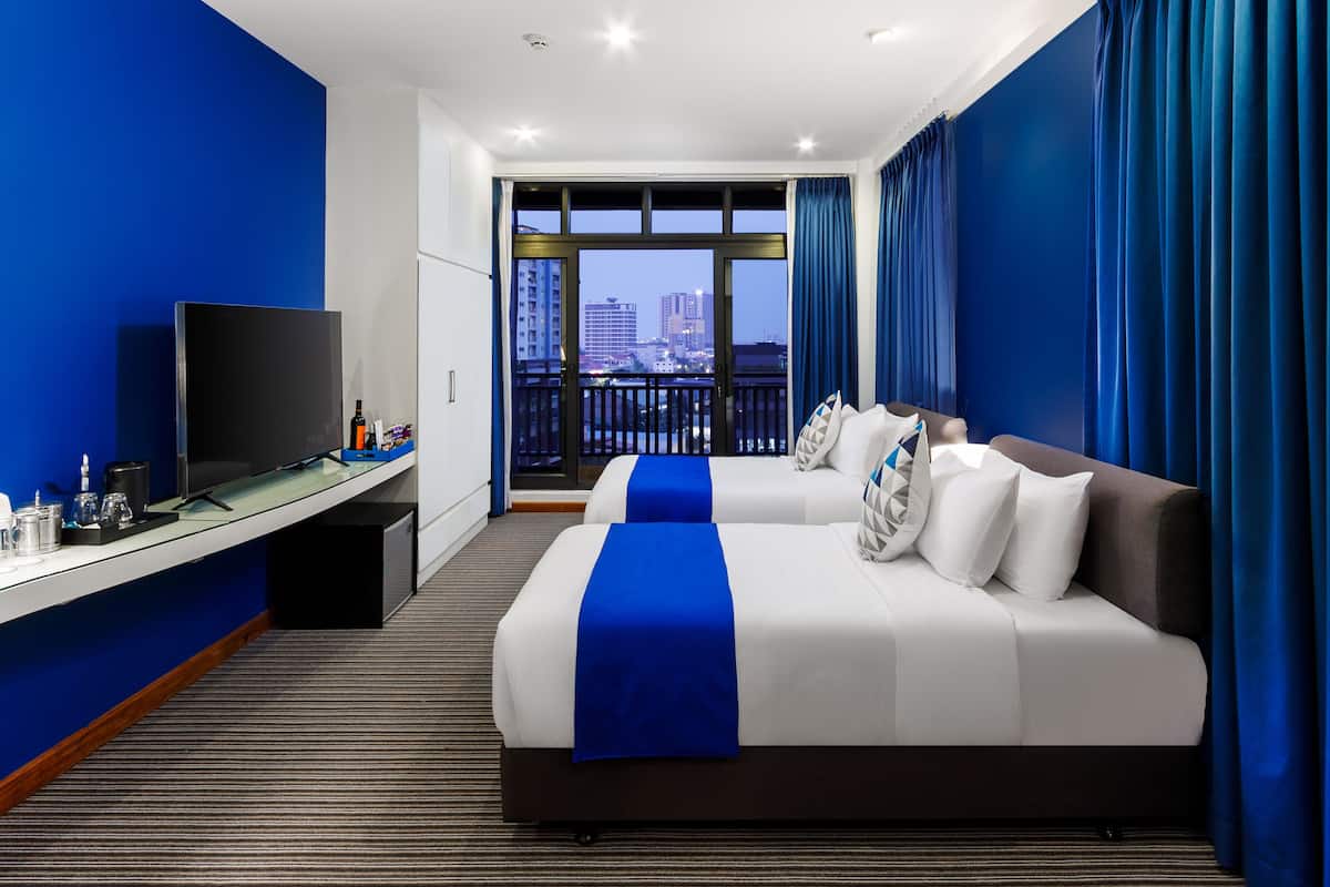 Quarto de hotel com uma cama grande, televisão, secretária com computador e varanda com vista para a cidade.