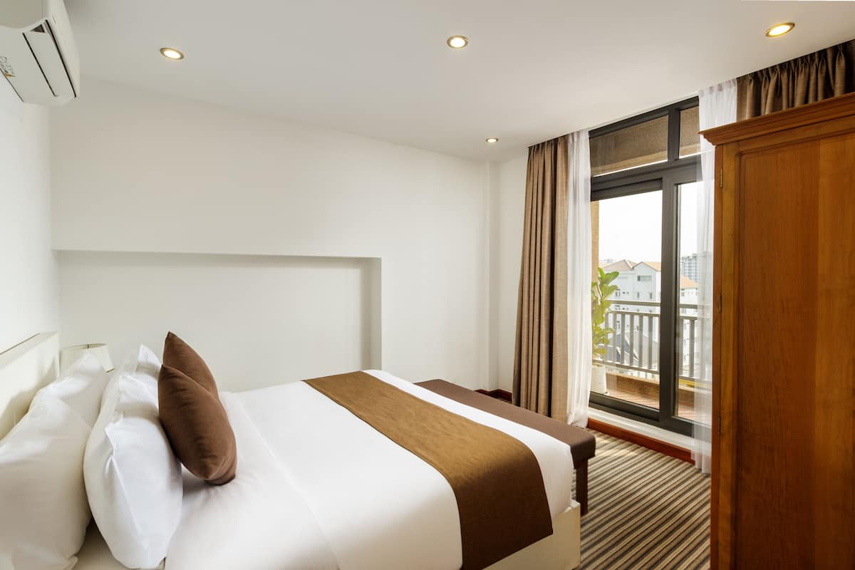 Quarto de hotel com uma cama grande, um guarda-roupa de madeira, uma janela com vista e iluminação embutida no teto.