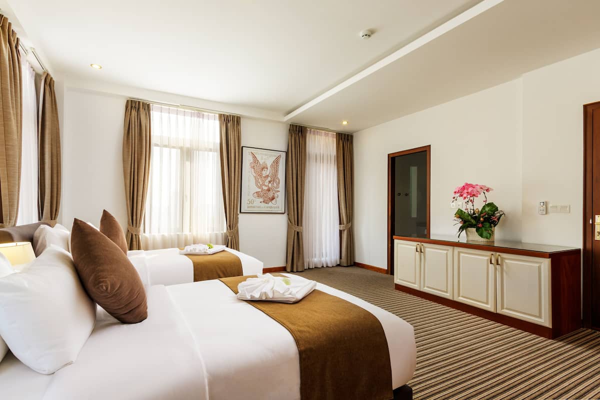 Quarto de hotel com duas camas, uma mesa, um espelho e uma janela com cortinas.