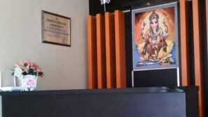 Uma área de recepção com um quadro de uma divindade, um certificado na parede e um vaso com flores.