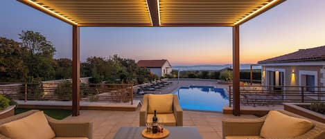Uma área externa coberta com piscina, móveis de vime e vista para a paisagem.