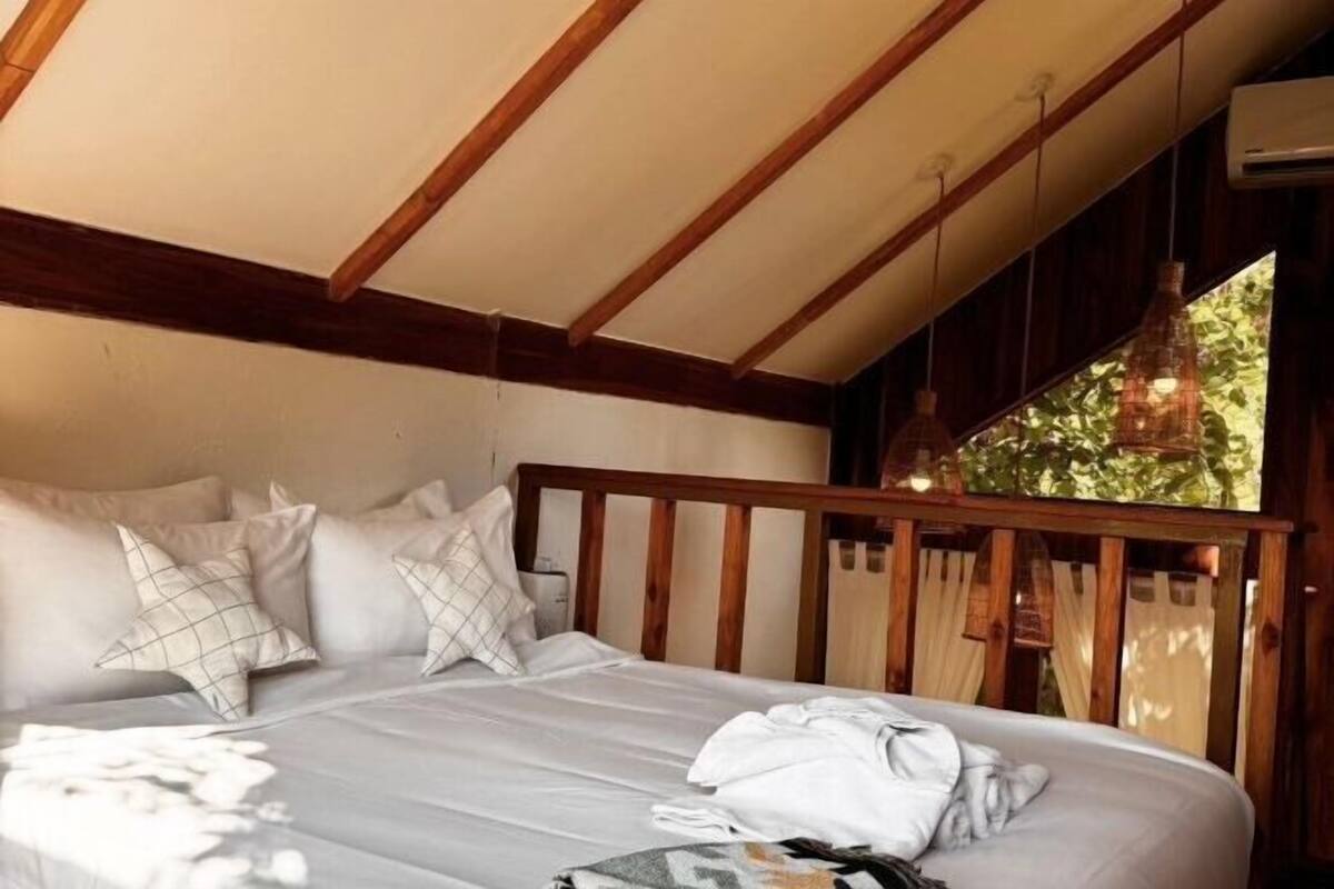 Uma cama com lençóis e almofadas brancas, cabeceira de madeira e luminária pendente.