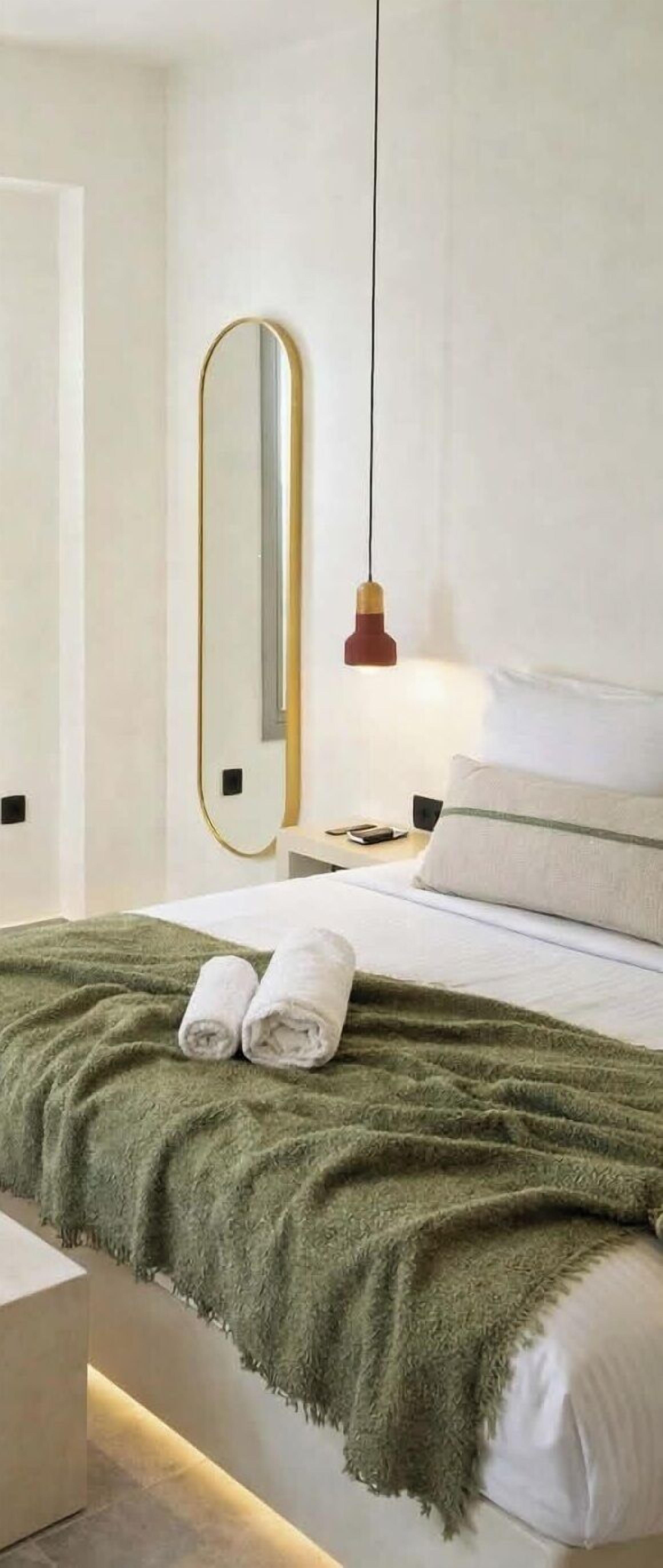 Quarto moderno com cama, um espelho grande e uma luminária pendente.