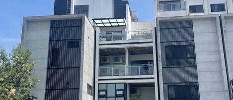 Um edifício moderno com fachada branca, várias varandas e entrada com portão.