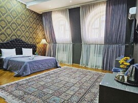 Quarto de hotel com cama, escrivaninha, cadeira, abajur e janela com cortinas.