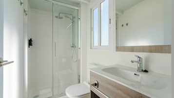 Uma casa de banho moderna com chuveiro envidraçado, sanita branca e lavatório com toucador de madeira.