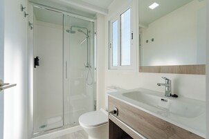 Uma casa de banho moderna com chuveiro envidraçado, sanita branca e lavatório com toucador de madeira.