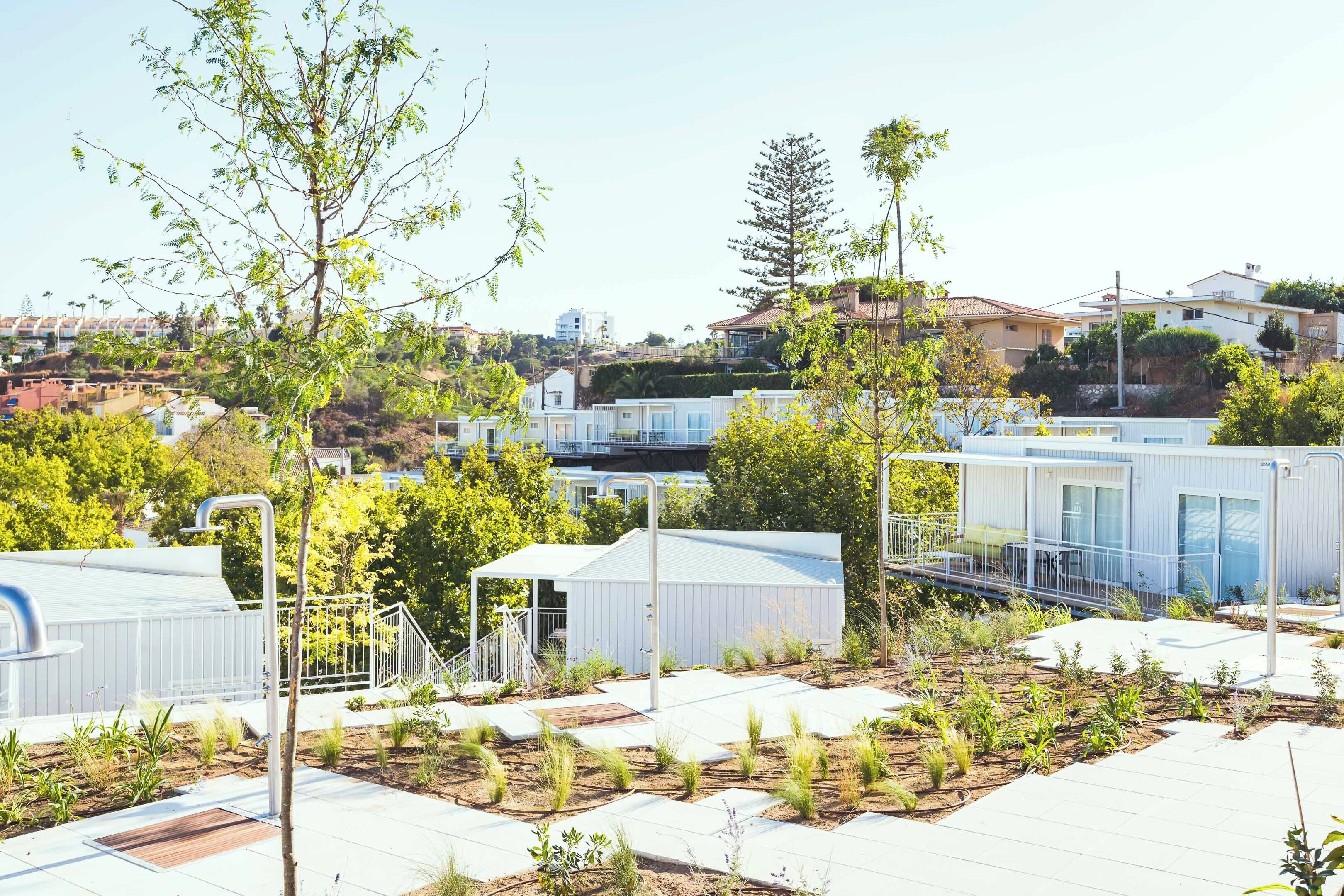 Zona residencial com casas modernas, um jardim com diversas plantas e céu claro.