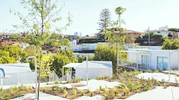 Zona residencial com casas modernas, um jardim com diversas plantas e céu claro.