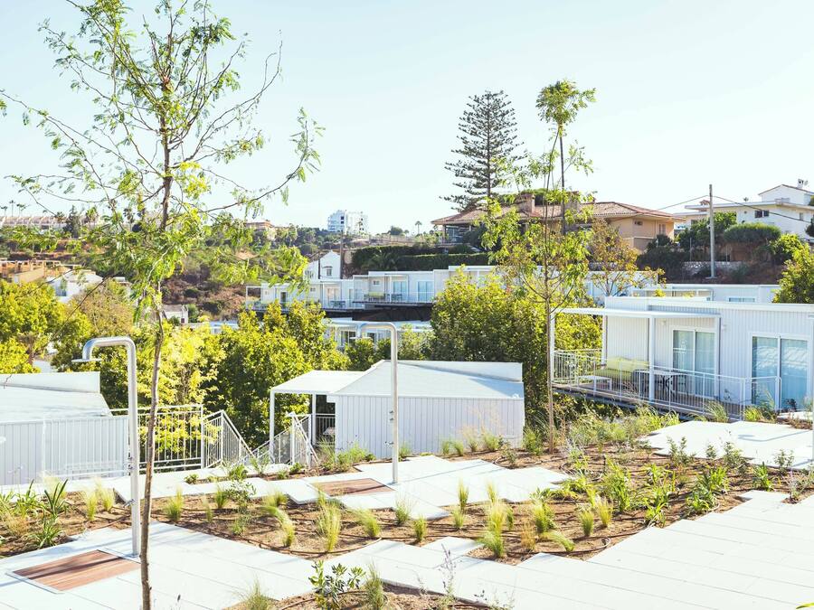 Zona residencial com casas modernas, um jardim com diversas plantas e céu claro.