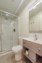 Uma casa de banho moderna com chuveiro de vidro, sanita branca e toucador bege com espelho.