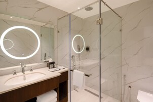 Uma casa de banho moderna com duas pias, um espelho grande com iluminação circular e cabine de duche com paredes de vidro.