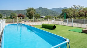 Piscina com área de grama sintética verde, cercada por uma cerca branca, com montanhas ao fundo.