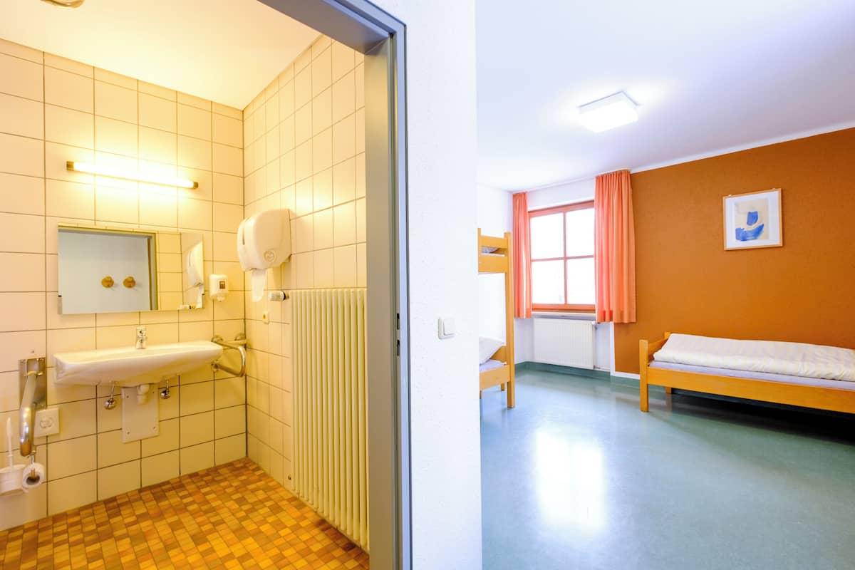Casa de banho com lavatório, espelho e sanita, e quarto com cama e janela.