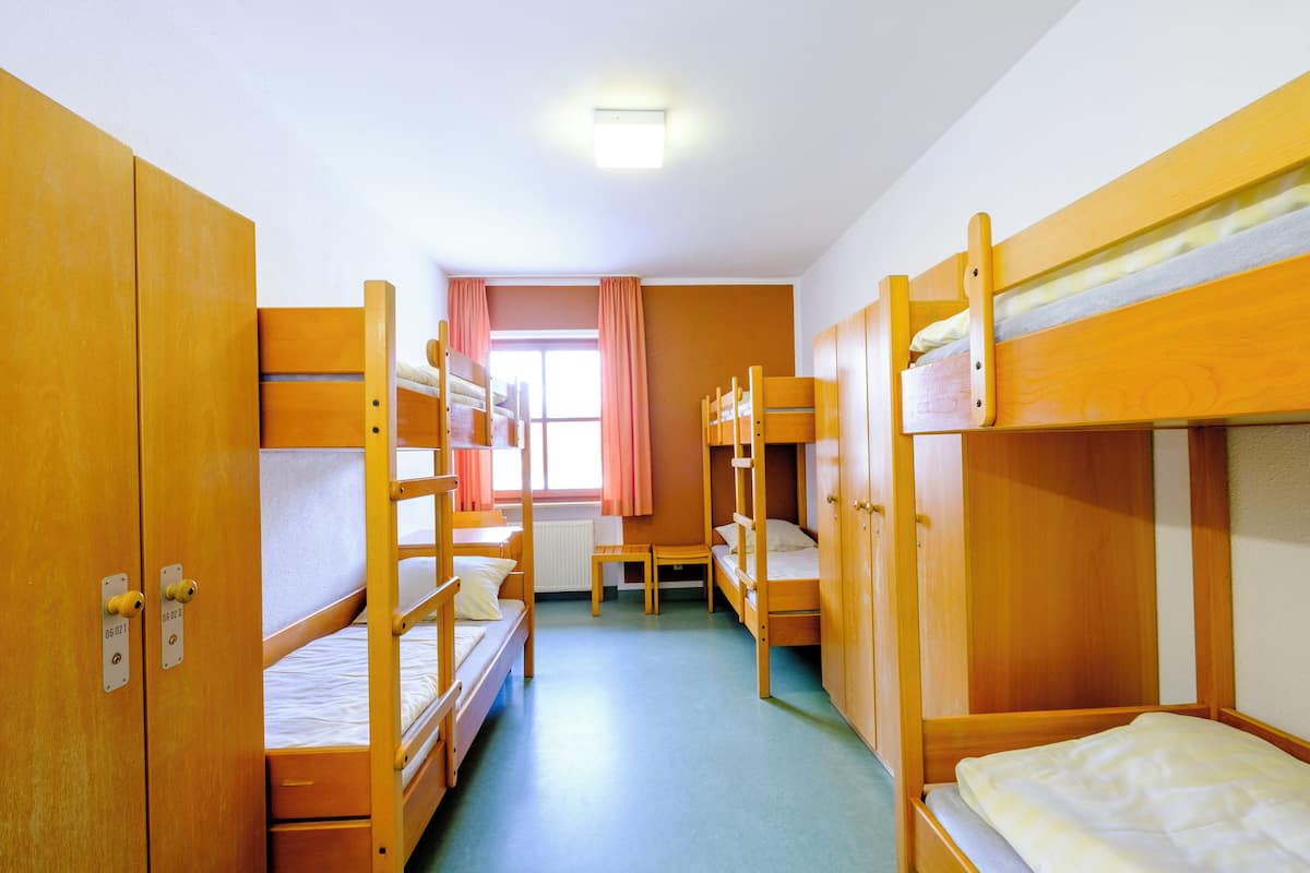 Quarto de dormitório com beliches, janela com cortinas e radiador.