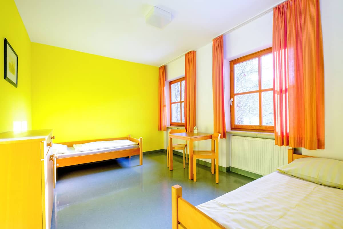 Quarto com cama, escrivaninha e cadeira, com janela e cortinas.