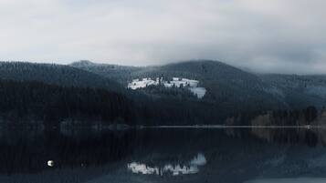 Vista tranquila de um lago, com uma montanha coberta de neve e um edifício no topo de uma colina.