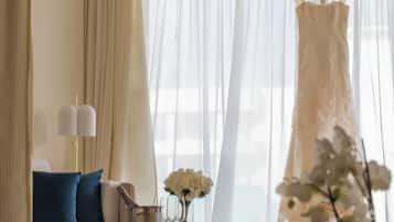 Quarto com um vestido pendurado, um sofá, uma mesa com livros e um vaso, e uma luminária no teto.