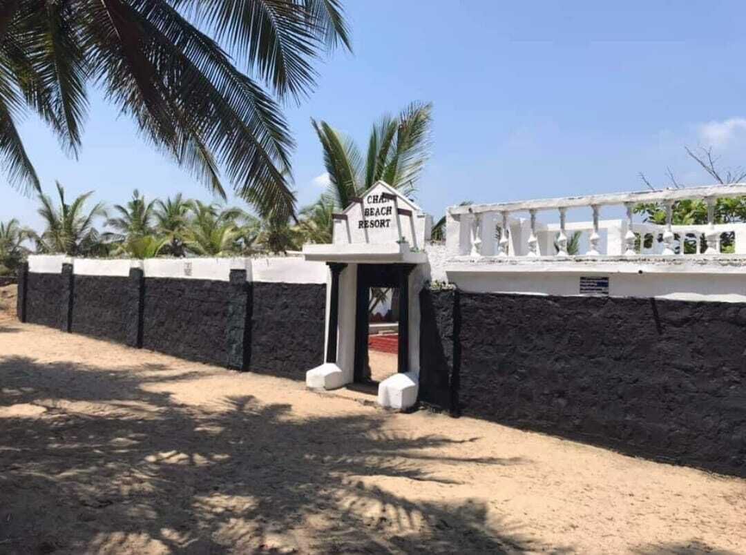 Entrada de um resort à beira-mar, com uma placa, muro de pedra e cerca branca.