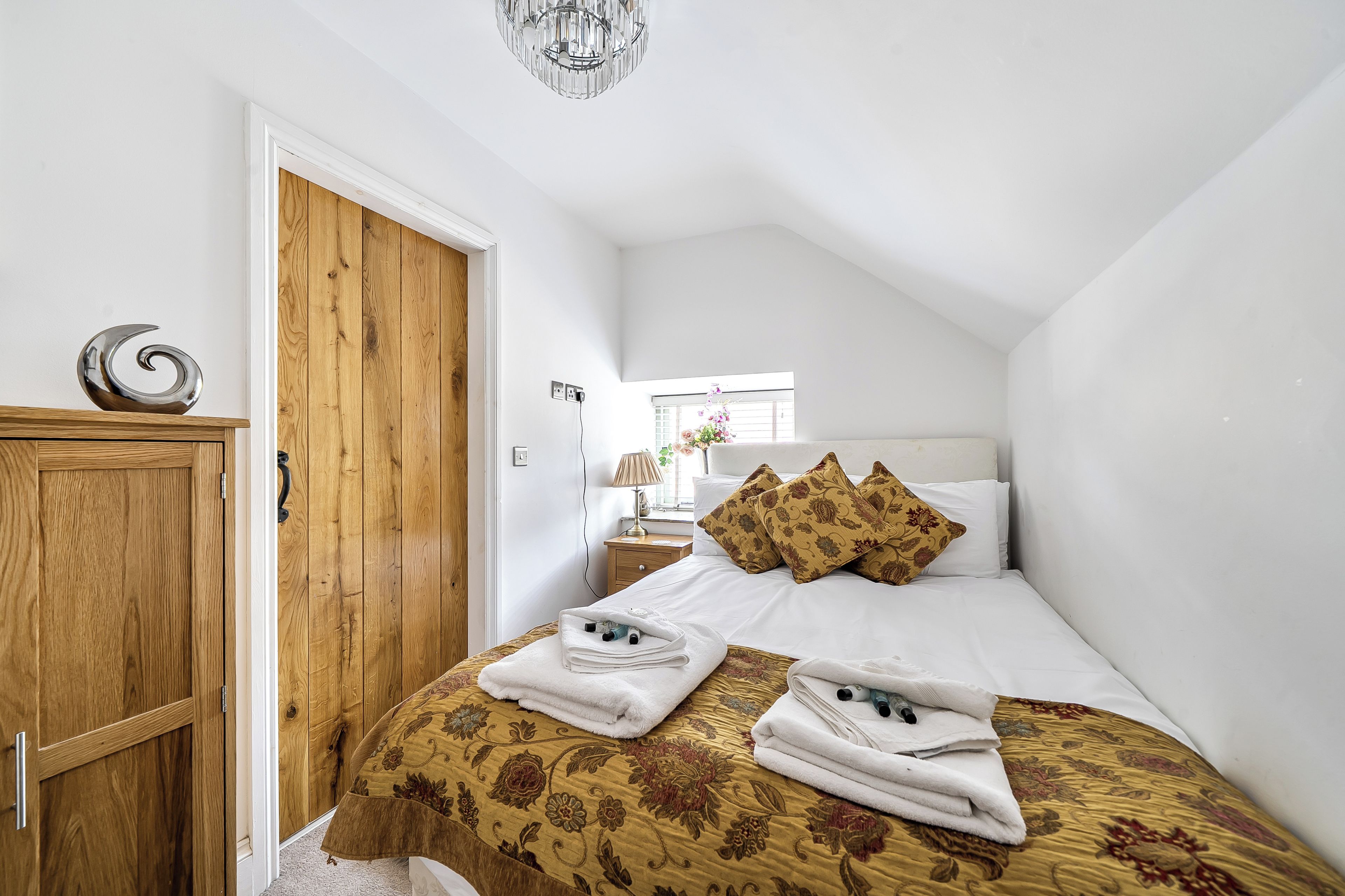 Quarto com cama, almofadas, mesa de cabeceira, abajur e guarda-roupa de madeira.