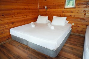 Quarto de cabana de madeira com uma cama, duas almofadas e um candeeiro fixado na parede.