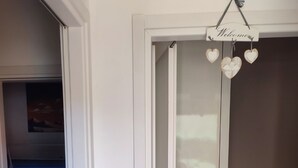 Quarto com cama, mesa de cabeceira e um criado-mudo. Uma porta dá acesso a um banheiro com chuveiro e vaso sanitário.