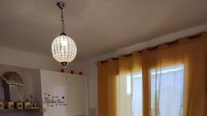 Cozinha compacta com armário branco, luminária pendente e janela com cortinas translúcidas.