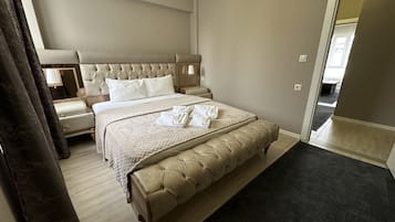 Quarto de hotel com uma cama grande, mesa de cabeceira, luminária e vista para o corredor.