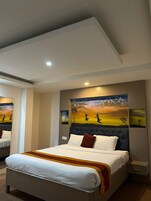 Quarto de hotel moderno com uma cama grande, cabeceira com pintura e mesa de cabeceira com abajur.