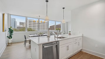 Uma cozinha moderna com uma ilha grande, armários brancos e vista para edifícios por grandes janelas.