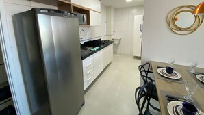 Uma cozinha moderna com geladeira de aço inoxidável, armários brancos e um espaço de refeições com mesa posta para dois.