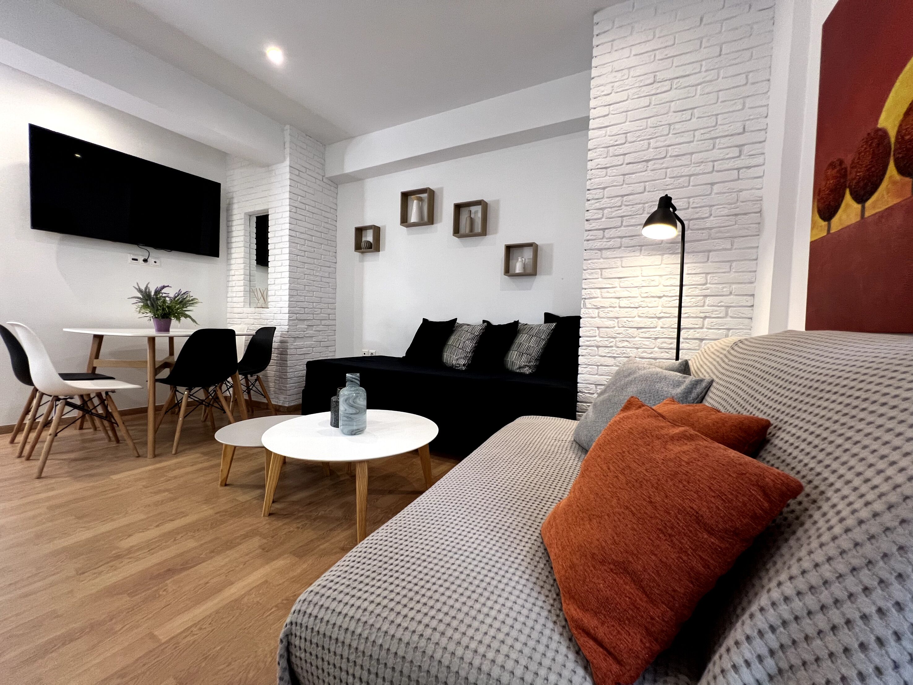 Uma sala de estar moderna com um sofá preto, um sofá cinza com almofadas laranja, uma mesa de centro branca e uma TV preta na parede.