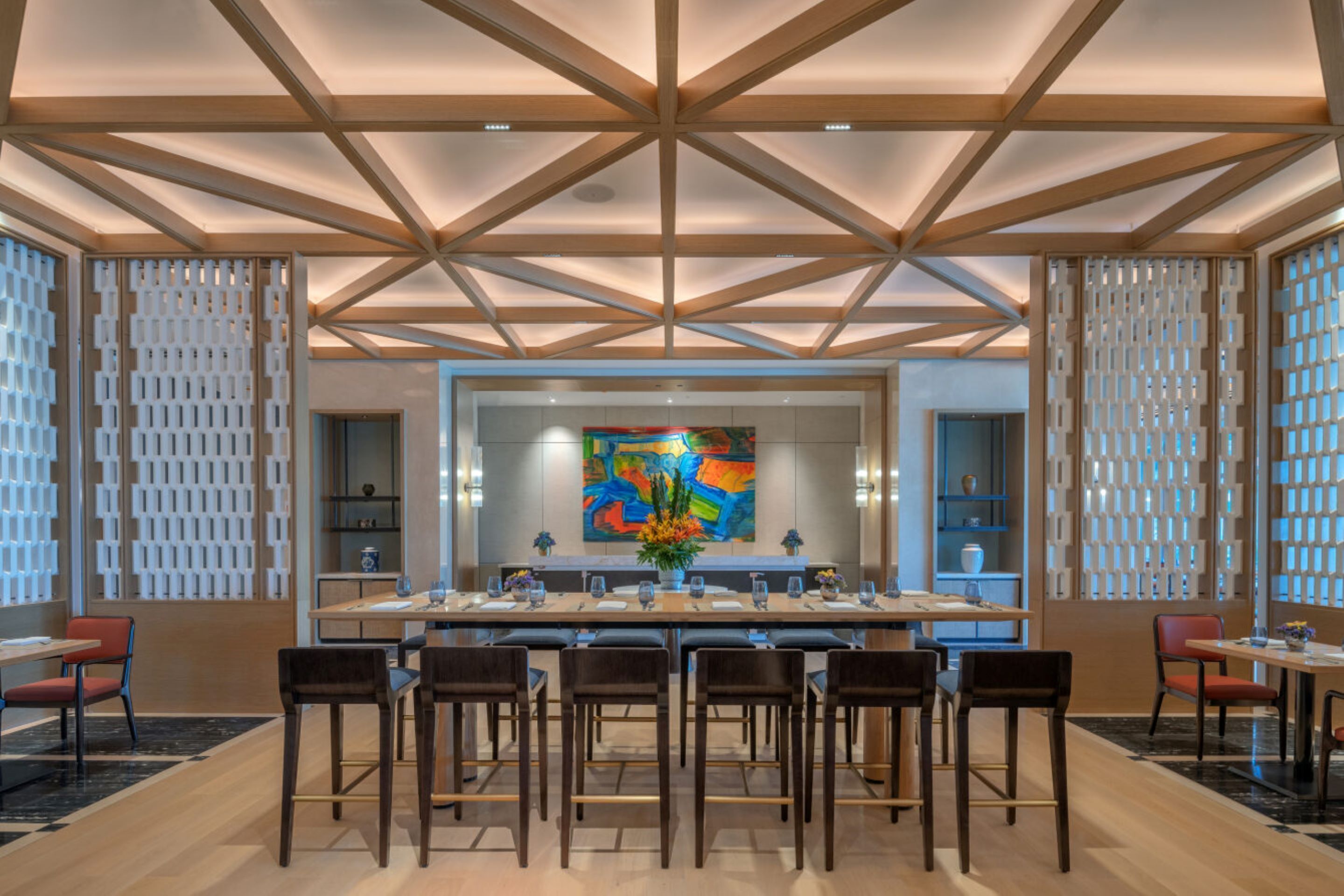 Uma sala de jantar moderna com uma mesa comprida, várias cadeiras e uma peça de arte central.