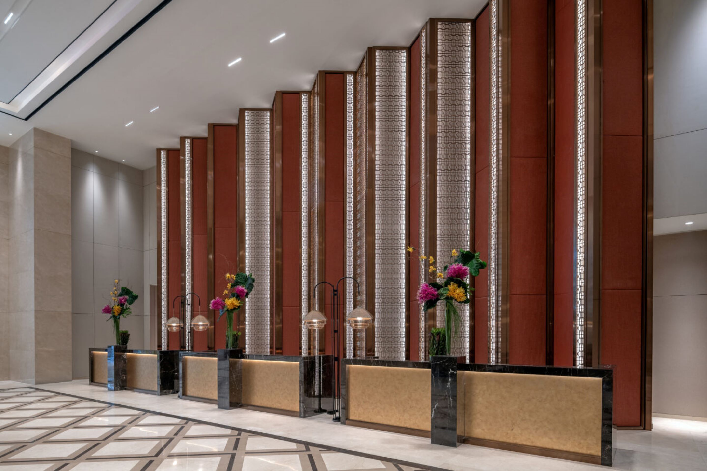 Uma área de recepção com design moderno, destacando um balcão longo, painéis decorativos verticais e plantas em vasos.